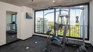 Uma academia com equipamentos de ginástica, esteira e uma grande janela com vista para a cidade.