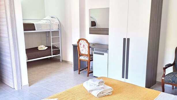 A hotel room with a bunk bed, a desk with a chair, a wardrobe, and a bed with towels.
