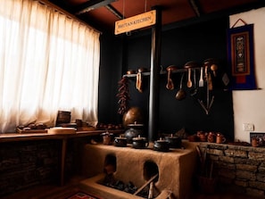 Uma cozinha tradicional com uma placa que diz 'Bhutan Kitchen', apresentando um fogão, panelas e utensílios.