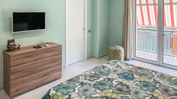 Quarto com cama, penteadeira, televisão e janela com vista para prédios.