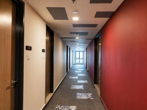 Corredor de hotel com piso de azulejos, portas em ambos os lados e uma parede vermelha.