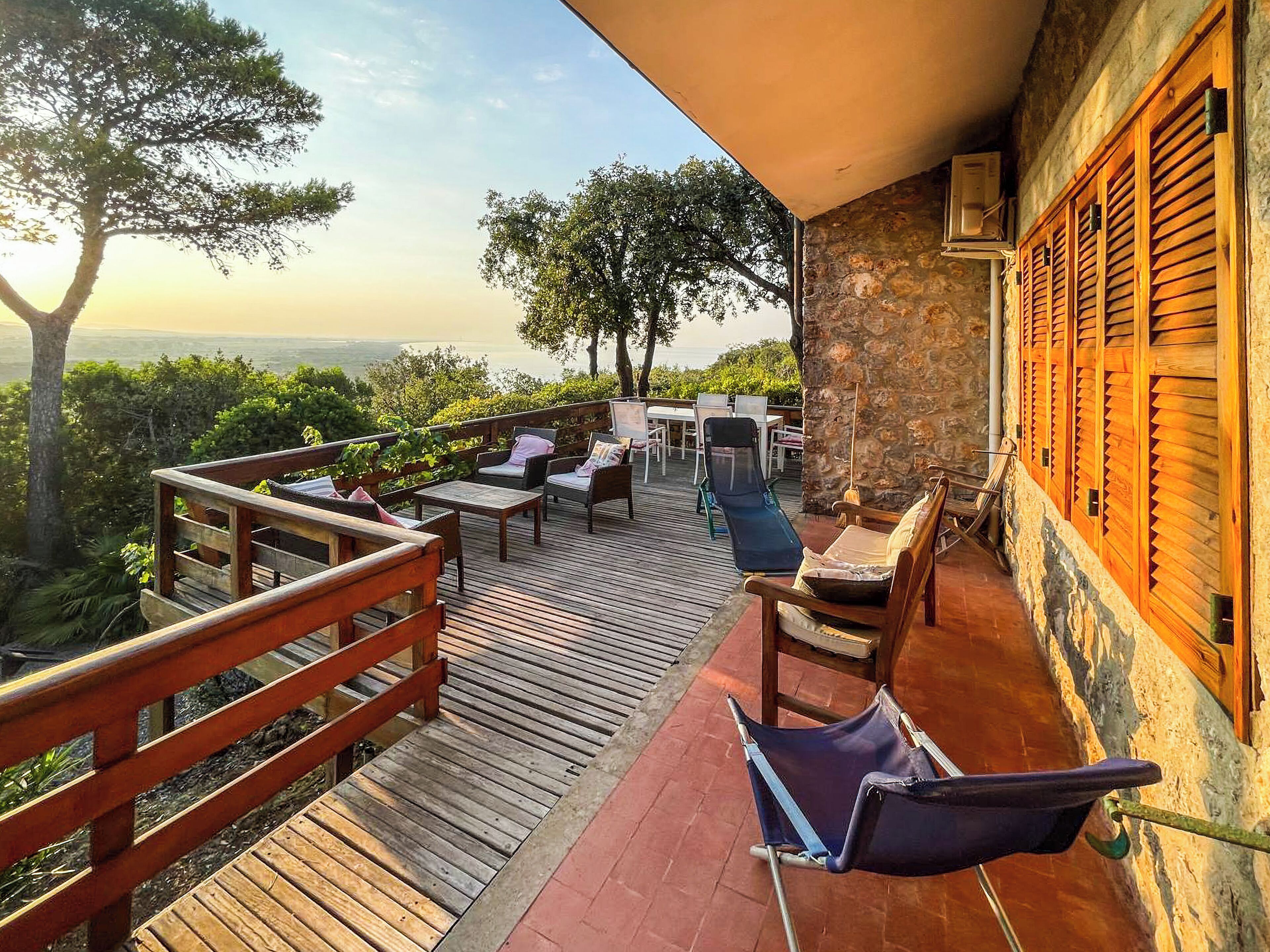 Um deck de madeira com mobiliário de exterior, uma parede de pedra e vista para a paisagem.