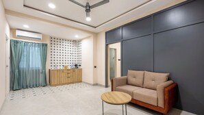 Uma sala de estar moderna com sofá, mesinha, ventilador de teto e uma área de cozinha com armário e painel de azulejos.