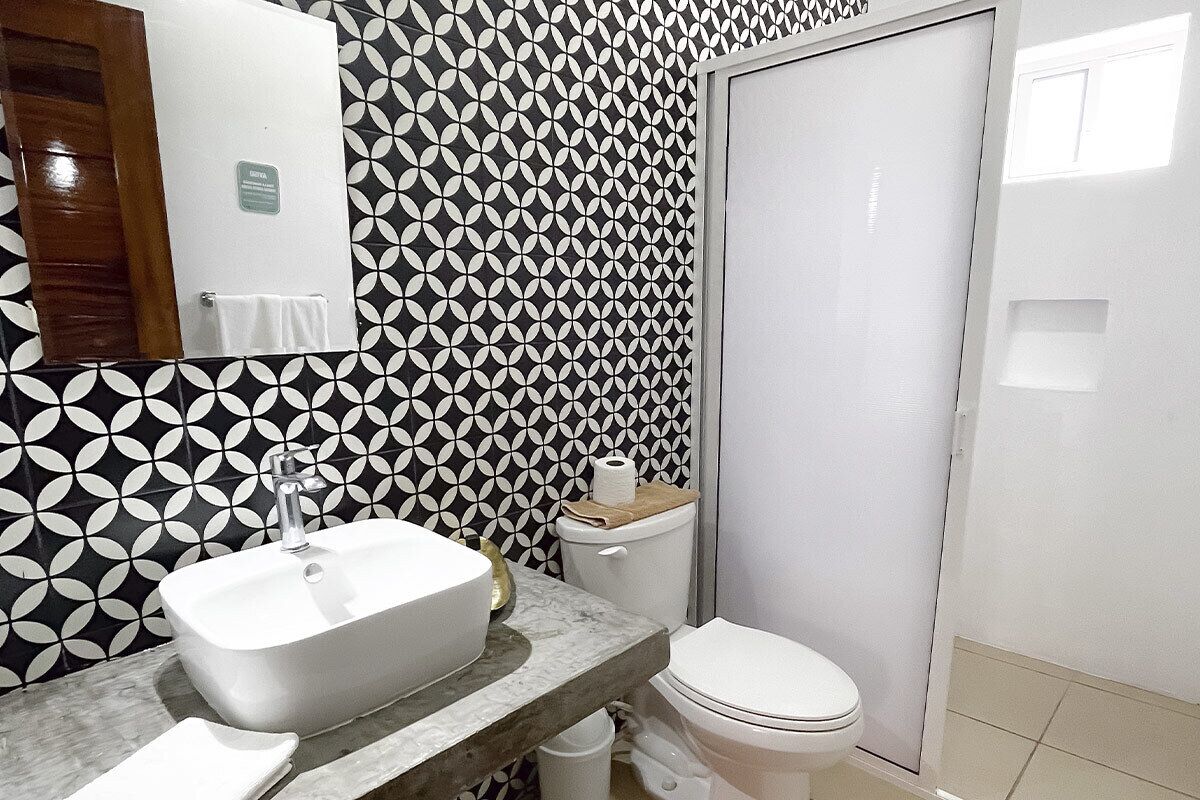 Casa de banho com lavatório branco, sanita e parede com padrão.
