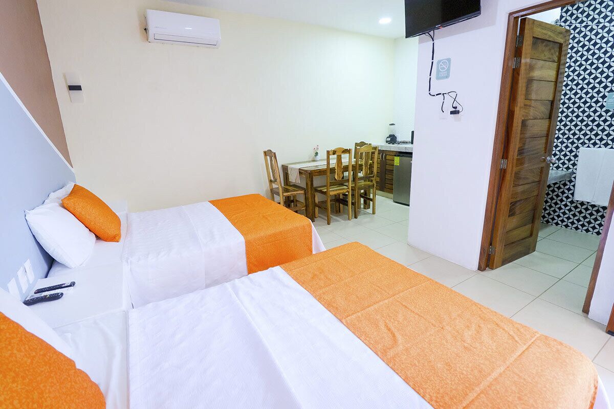 Quarto de hotel com duas camas, área de refeições e cozinha compacta.