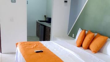 Quarto com cama, colcha laranja e três almofadas laranjas.