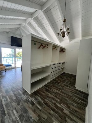 Um quarto com teto inclinado, piso de madeira e uma estante embutida com cabides.