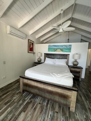Um quarto com uma cama de madeira, um ventilador de teto e um quadro na parede.