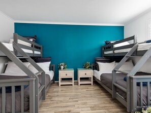 Quarto com beliches, uma mesinha de cabeceira com uma planta e parede pintada em tom azul-turquesa.