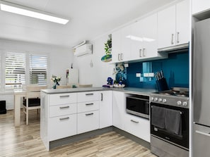 Cozinha moderna com armários brancos, fogão de aço inoxidável e painel de fundo azul.