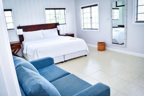 Quarto com cama, mesa de cabeceira, sofá azul, janela e espelho fixado na parede.