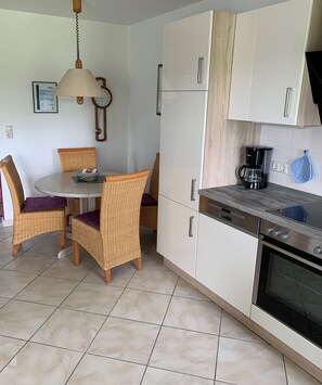 Uma cozinha compacta com área de jantar, com uma mesa redonda, cadeiras de vime, cafeteira e forno embutido.