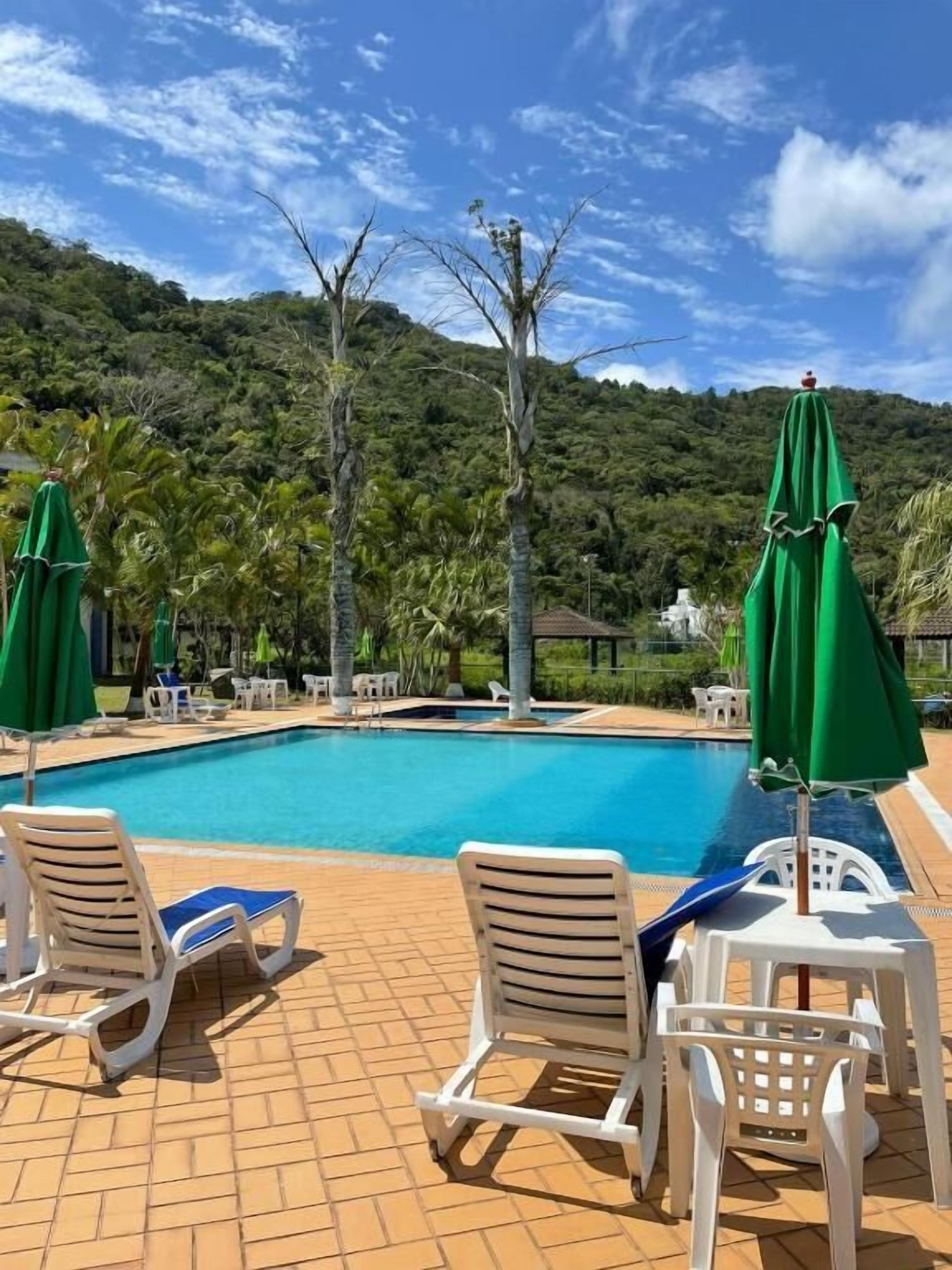Piscina com espreguiçadeiras e guarda-sóis, cercada por vegetação e paisagem montanhosa.