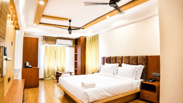 Quarto de hotel com uma cama grande, piso de madeira, ventilador de teto, ar condicionado, mesa de cabeceira e uma escrivaninha.