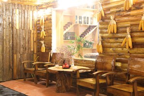 Interior rústico de madeira, com uma mesa redonda, quatro cadeiras de madeira e um vaso com flores.