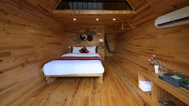 Interior de uma cabana de madeira, com uma cama, um mezanino e uma pequena cozinha.