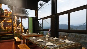 Uma sala de jantar com mesa posta para quatro pessoas, grandes janelas com vista para a montanha e uma escada com corrimão.