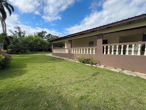 Edifício residencial com varanda coberta, gramado bem cuidado e vegetação ao redor.