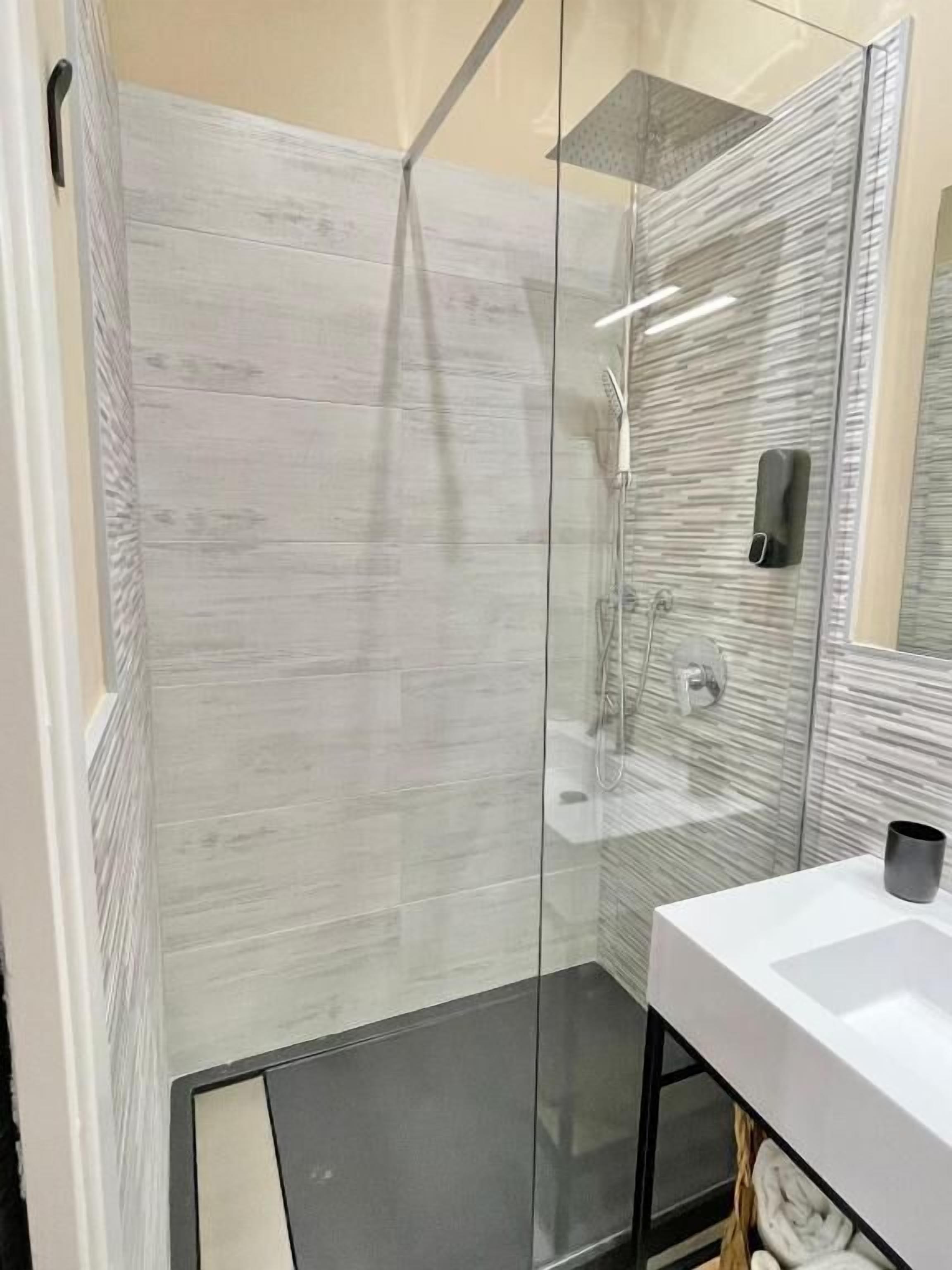 Uma casa de banho moderna com chuveiro em cabine de vidro, lavatório branco e espelho.