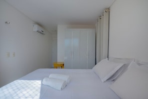Quarto com cama, uma mesinha, guarda-roupa e ar condicionado.
