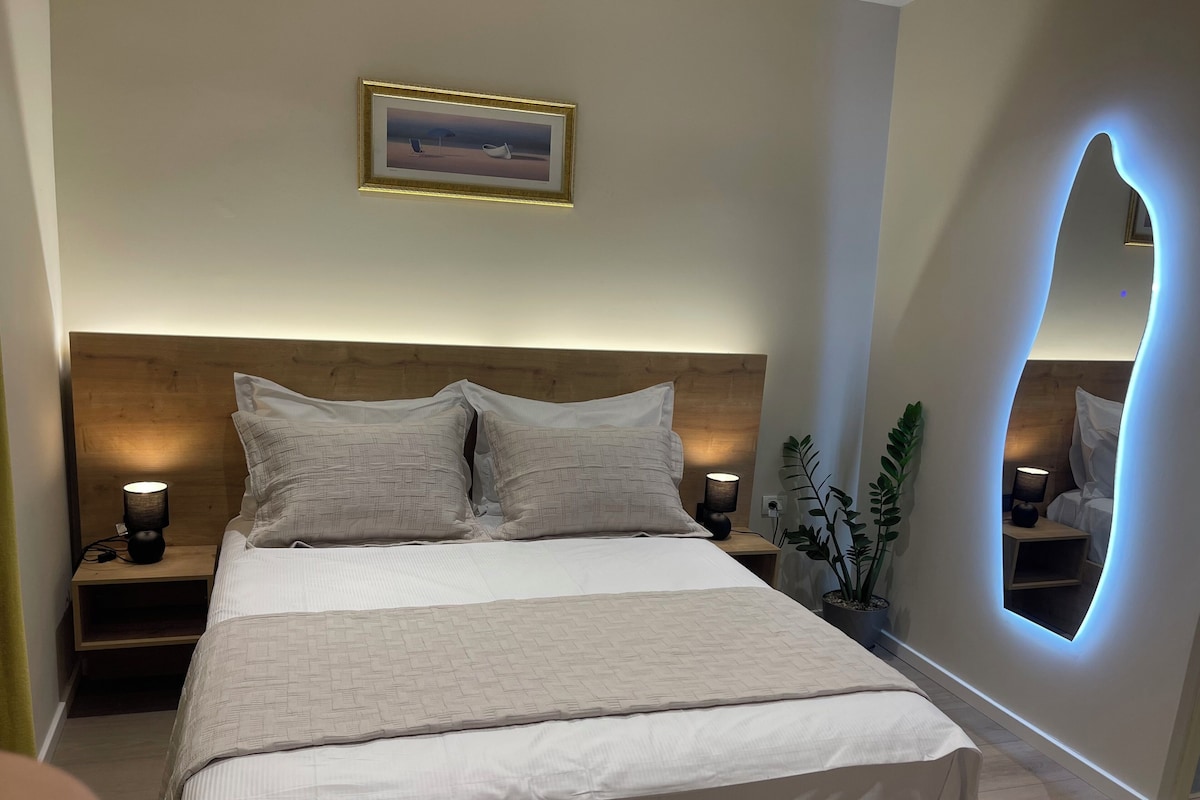 Um quarto moderno com cabeceira de madeira, uma cama grande com roupa de cama branca, duas luminárias de cabeceira e um quadro na parede.