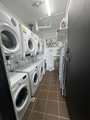 Uma lavanderia com várias máquinas de lavar, uma pia e um cesto de lixo.