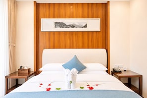 Quarto de hotel com cabeceira de madeira, um quadro emoldurado sobre a cama, almofada branca, almofada azul, toalha branca e manta azul.