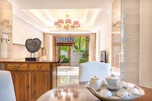 Quarto de hotel moderno com uma escrivaninha de madeira, uma mesa de jantar com bules e uma porta de estilo tradicional, além de iluminação embutida no teto.