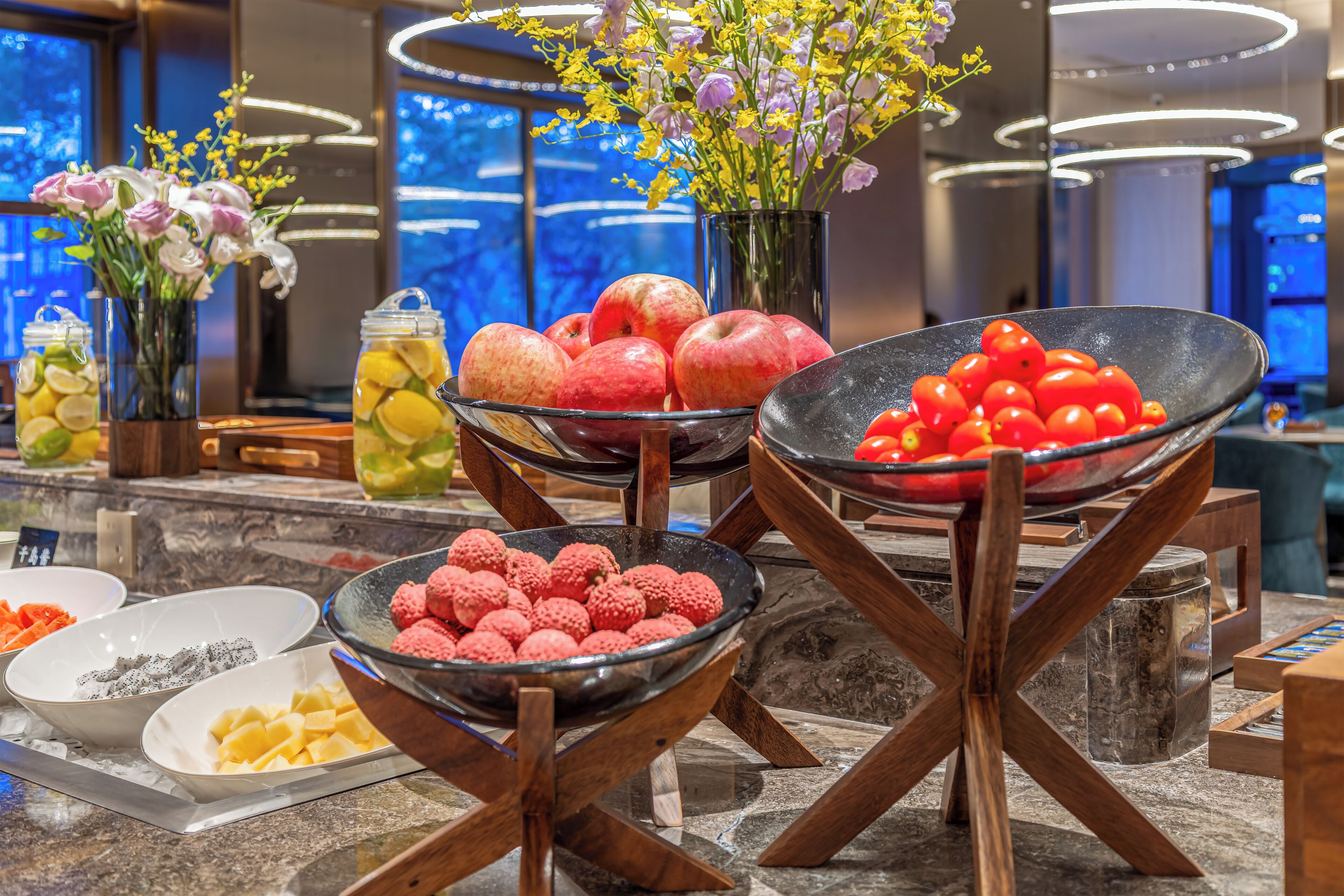 Disposição de buffet com diversas frutas e legumes, incluindo maçãs, tomates e framboesas, dispostos em uma bancada de mármore.