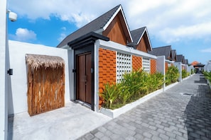 Uma área residencial moderna com um caminho pavimentado, uma porta de madeira e uma parede branca com telhado de palha.