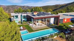 Uma casa moderna com piscina, painéis solares e vista para as colinas.