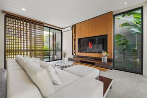 Uma sala de estar moderna com uma grande TV de tela plana, um sofá branco e um armário de madeira.