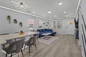 Uma sala de estar moderna com um sofá azul, uma mesa de jantar com cadeiras e um lustre.