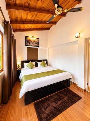 Quarto com teto de madeira, cama com manta verde, mesa de cabeceira com abajur e quadro pendurado na parede.