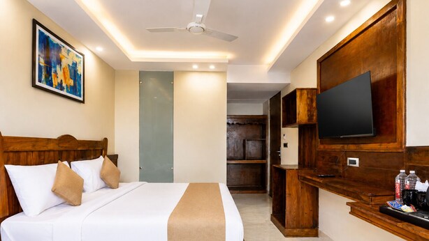 Quarto de hotel com cama, televisão, guarda-roupa e ventoinha no teto.