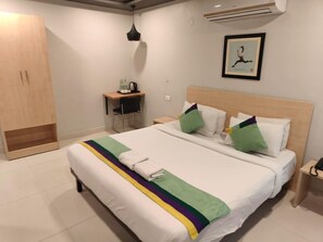 Quarto de hotel com uma cama grande, uma escrivaninha com cadeira, um guarda-roupa e um quadro pendurado na parede.