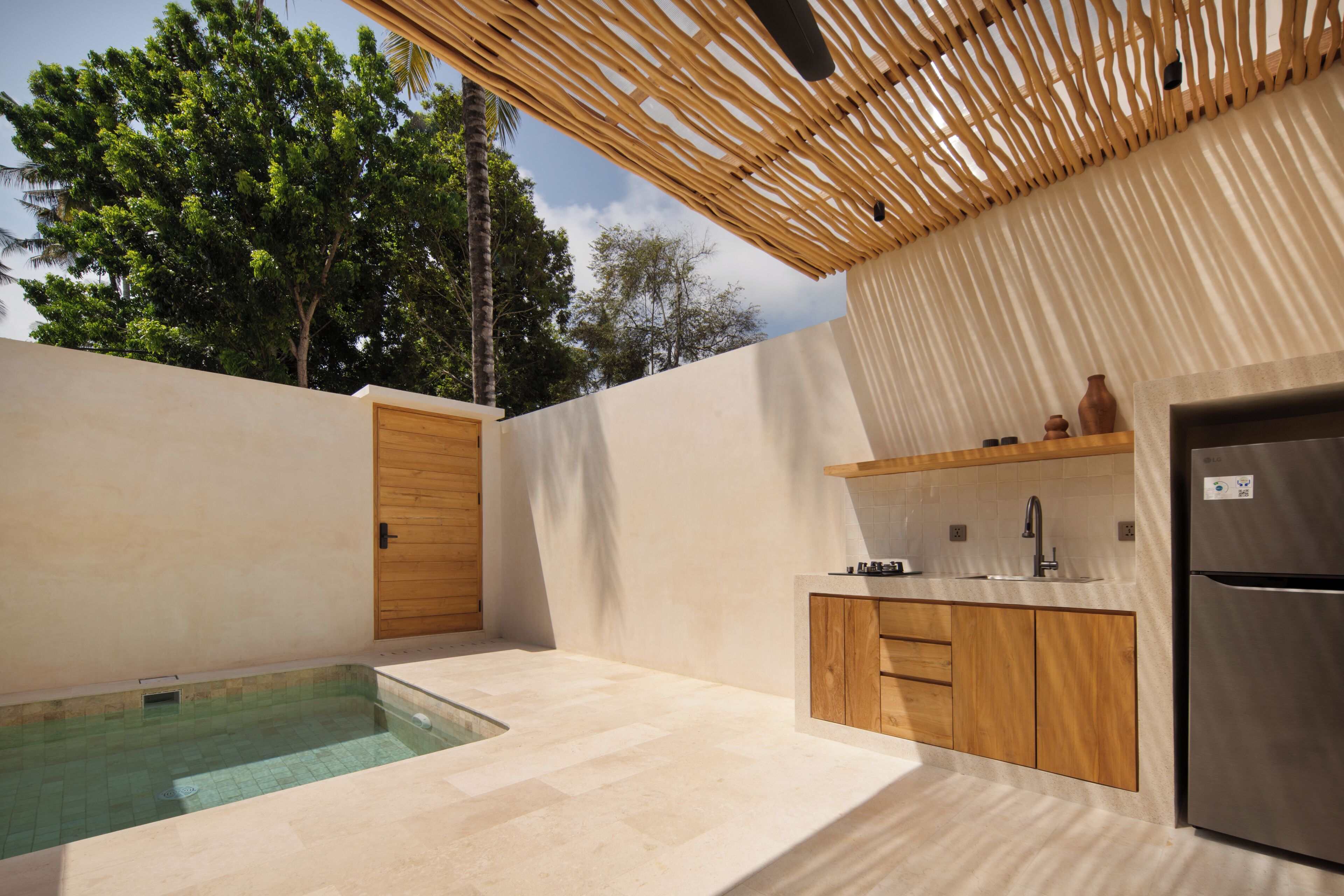 Cozinha externa moderna com piscina integrada, armários de madeira e geladeira de aço inoxidável.