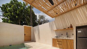 Cozinha externa moderna com piscina integrada, armários de madeira e geladeira de aço inoxidável.