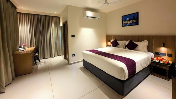 Quarto de hotel com uma cama grande, uma escrivaninha, uma cadeira, um ventilador de teto e um quadro na parede.