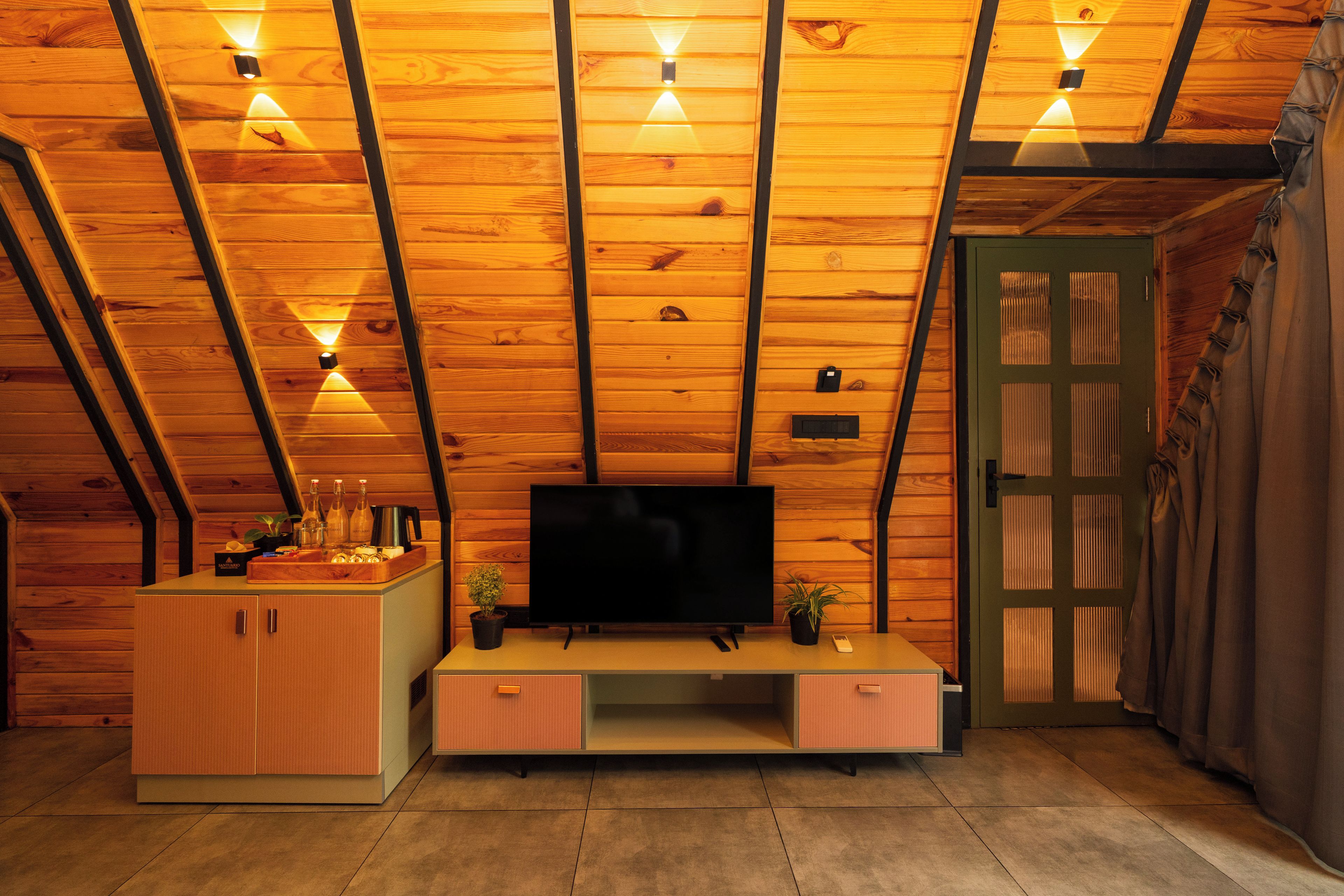 Quarto aconchegante com teto de madeira, televisão de tela plana em suporte de madeira, armário com gavetas e porta com janela.