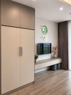 Uma sala de estar moderna com um guarda-roupa espaçoso, uma televisão de tela plana na parede, uma pequena planta e um vaso com galhos decorativos.