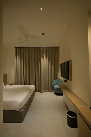Quarto de hotel com cama, uma cadeira, televisão na parede e ventilador de teto.