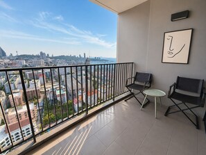 Varanda com vista para a cidade, duas cadeiras, uma mesa pequena e uma obra de arte emoldurada.