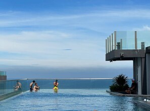 Piscina infinita no terraço, com vista clara do oceano, guarda-corpo de vidro e design arquitetônico moderno.