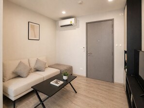 Uma sala de estar moderna com um sofá, uma mesa de centro, uma porta e um ar condicionado.