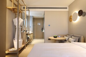Quarto de hotel com uma cama grande, uma mesa redonda com uma tigela, um sofá, um espelho e um guarda-roupa.