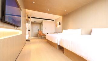 Quarto de hotel com cama, cadeira, escrivaninha e televisão presa na parede.