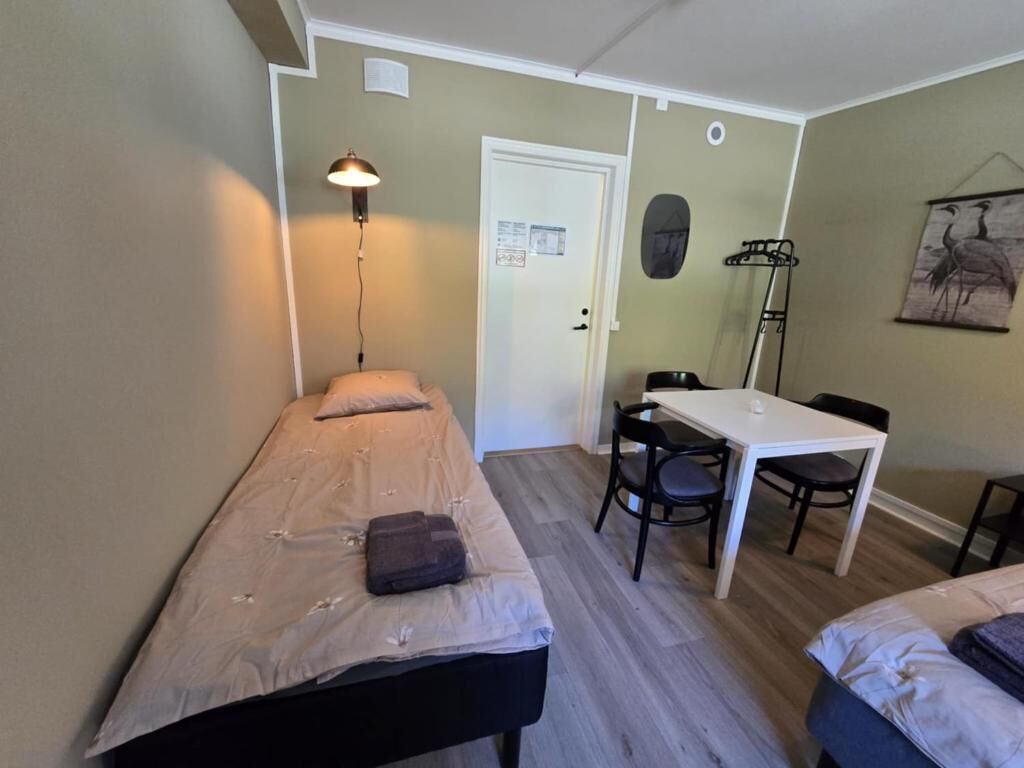 Quarto com duas camas, uma mesa, cadeiras, um abajur e uma porta.