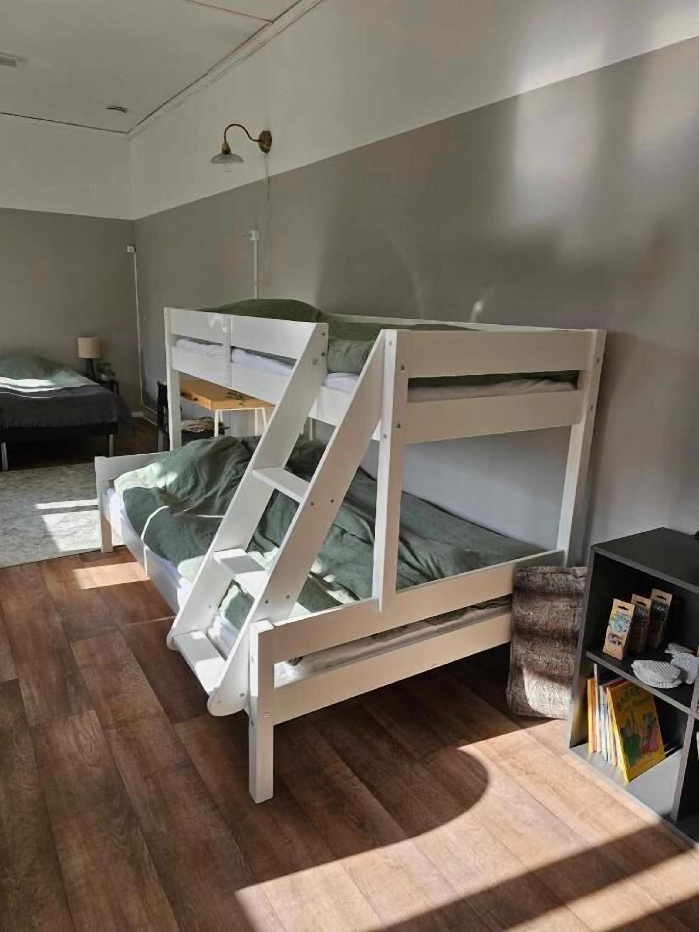 Uma cama de beliche com escada, uma mesinha de cabeceira, uma luminária e uma estante de livros.