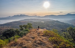 Uma pessoa em um morro, com vista para um vale, montanhas ao longe e um corpo d'água.